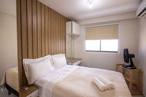 Quarto de hotel com cama, mesa de cabeceira, escrivaninha, cadeira, janela com vista e ar condicionado.