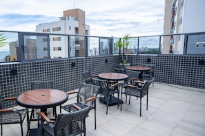 Terraço no telhado com mesas e cadeiras redondas, um vaso de planta e vista panorâmica da cidade.