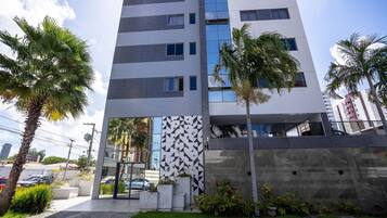 Um edifício moderno de vários andares com fachada geométrica, entrada de vidro e áreas verdes ao redor.