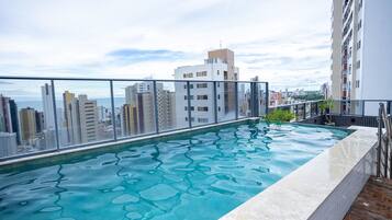 Piscina no terraço com vista para a cidade, cercada por edifícios altos.