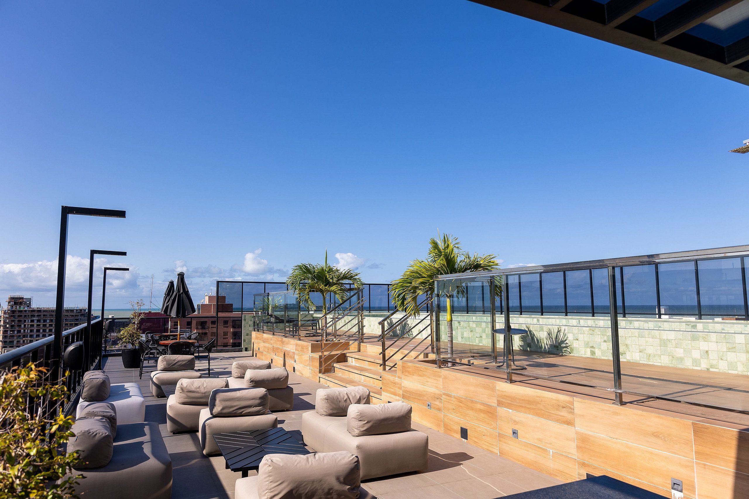 Terraço no telhado com área de estar ao ar livre, guarda-corpo de vidro e vista para o mar.