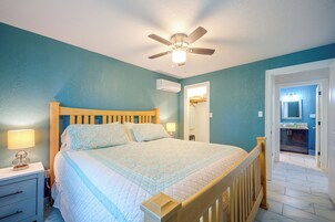 Quarto com cama, luminárias laterais, ventilador de teto e banheiro visível por uma porta aberta.