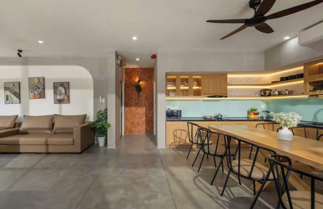Cozinha moderna com bancada de madeira, área de jantar com mesa comprida e cadeiras, e ventilador de teto.