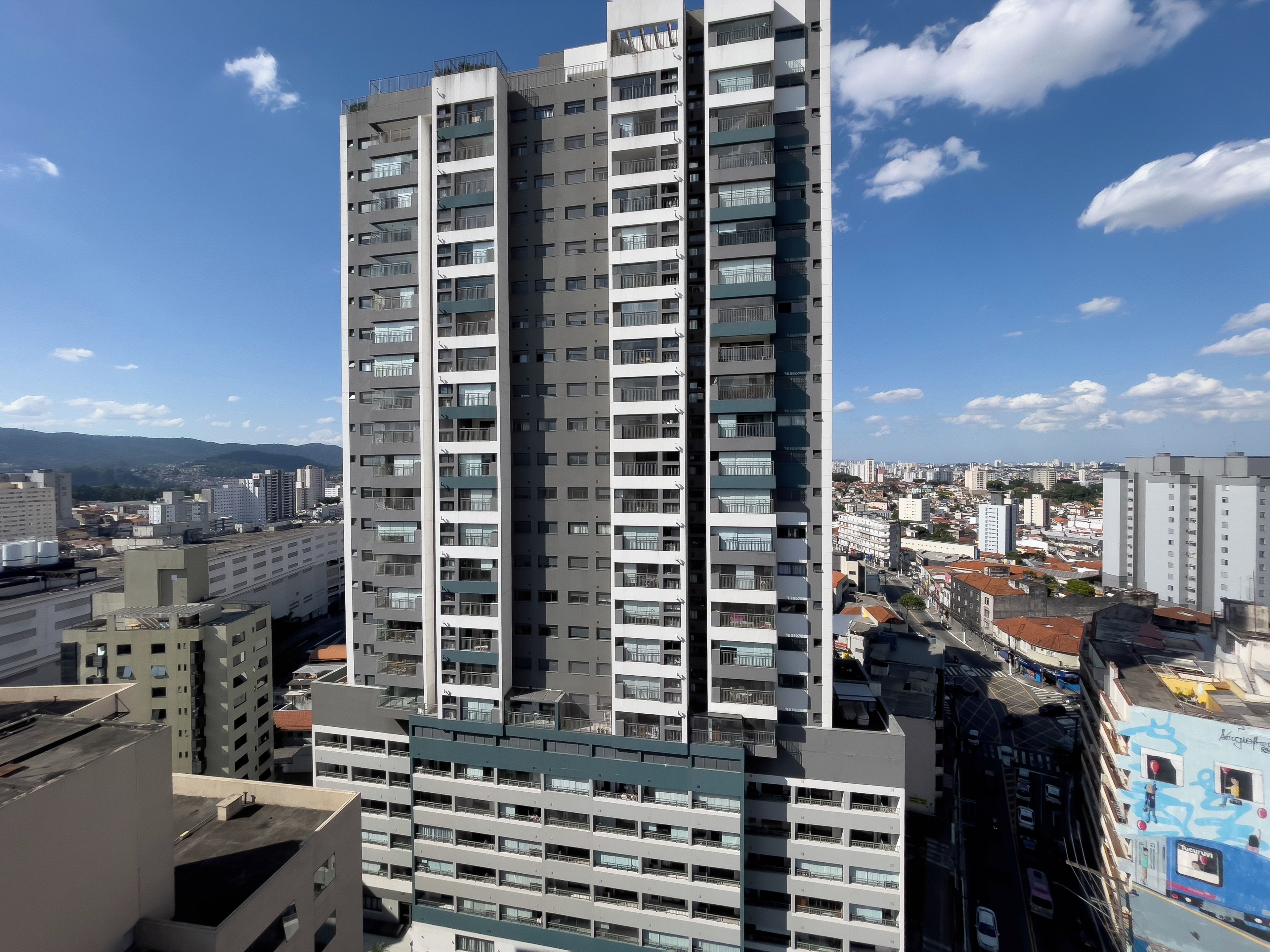 Um edifício alto com várias varandas, cercado por outros edifícios e um céu claro.