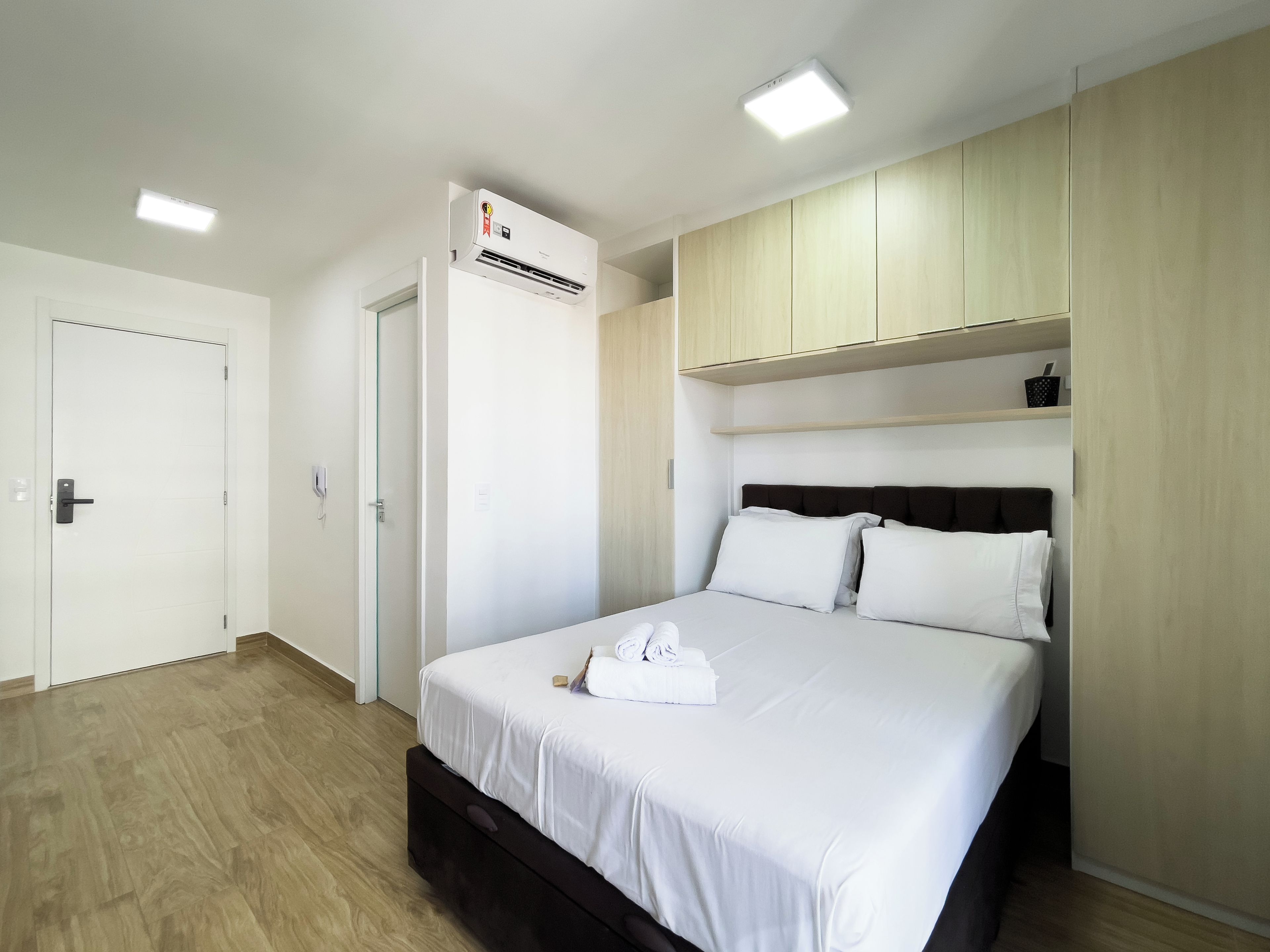 Quarto de hotel com cama, guarda-roupa, ar condicionado e uma porta.