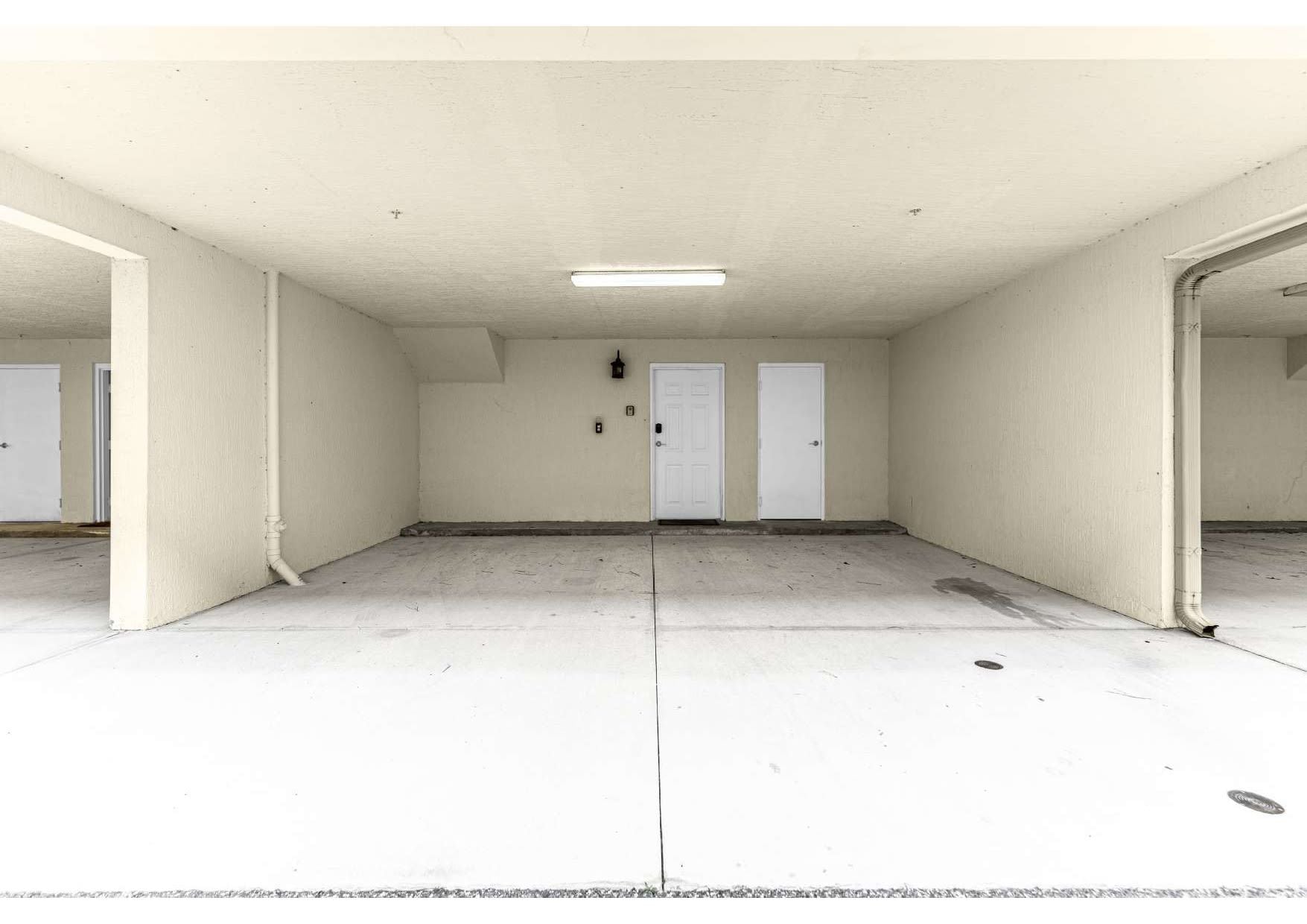 Quarto vazio com paredes brancas, teto plano e porta visível.