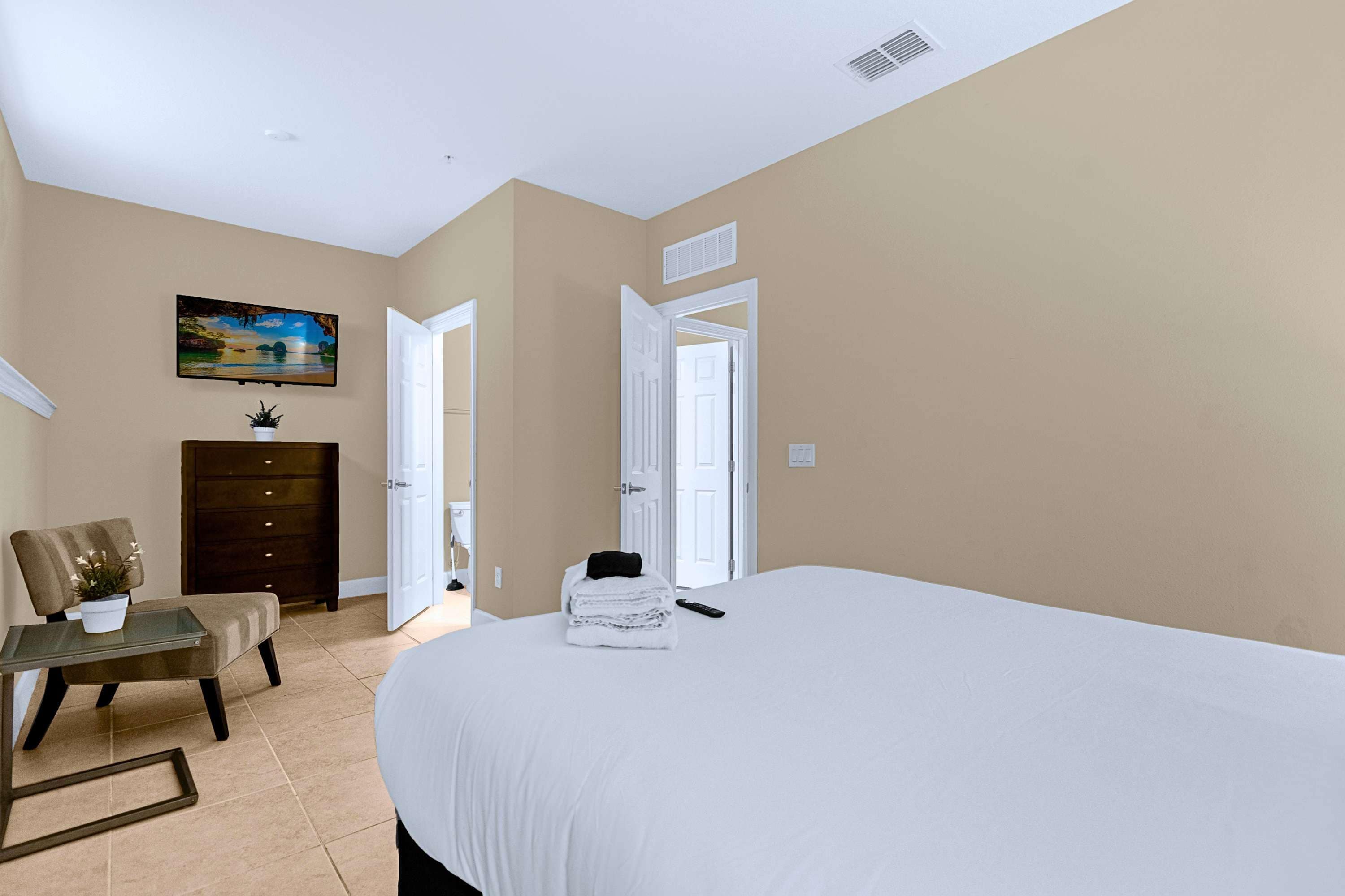 Quarto de hotel com uma cama grande, uma escrivaninha, uma cadeira, uma cômoda e um quadro na parede.
