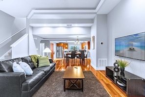 Uma sala de estar moderna com sofá de couro, mesa de centro de madeira e uma área de refeições, com cozinha ao fundo.