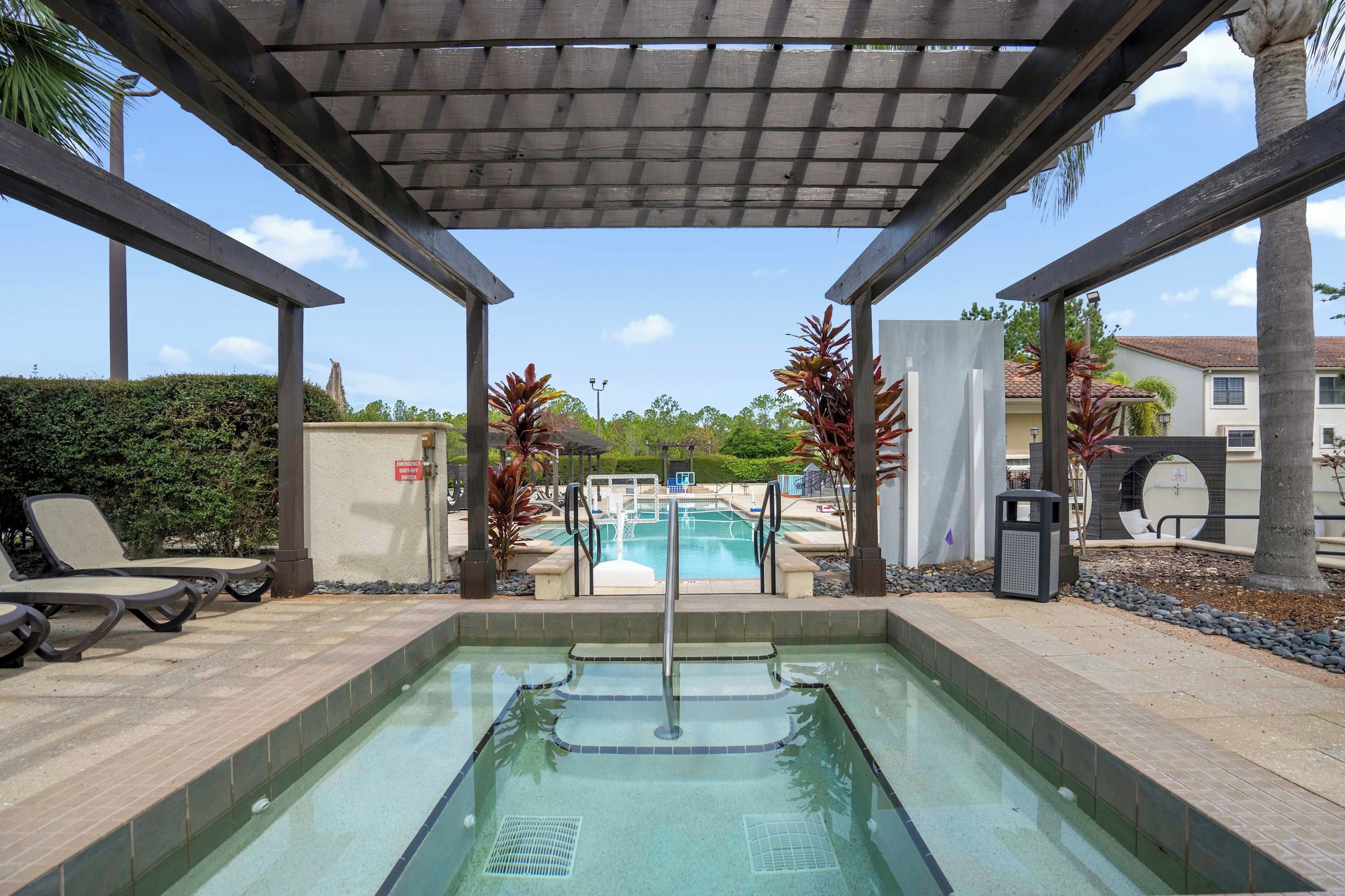 Uma área de piscina com pergolado, cadeiras de descanso e vista para a piscina.