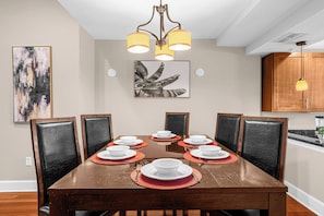 Uma sala de jantar com uma mesa de madeira posta para seis lugares, rodeada por cadeiras de couro preto.