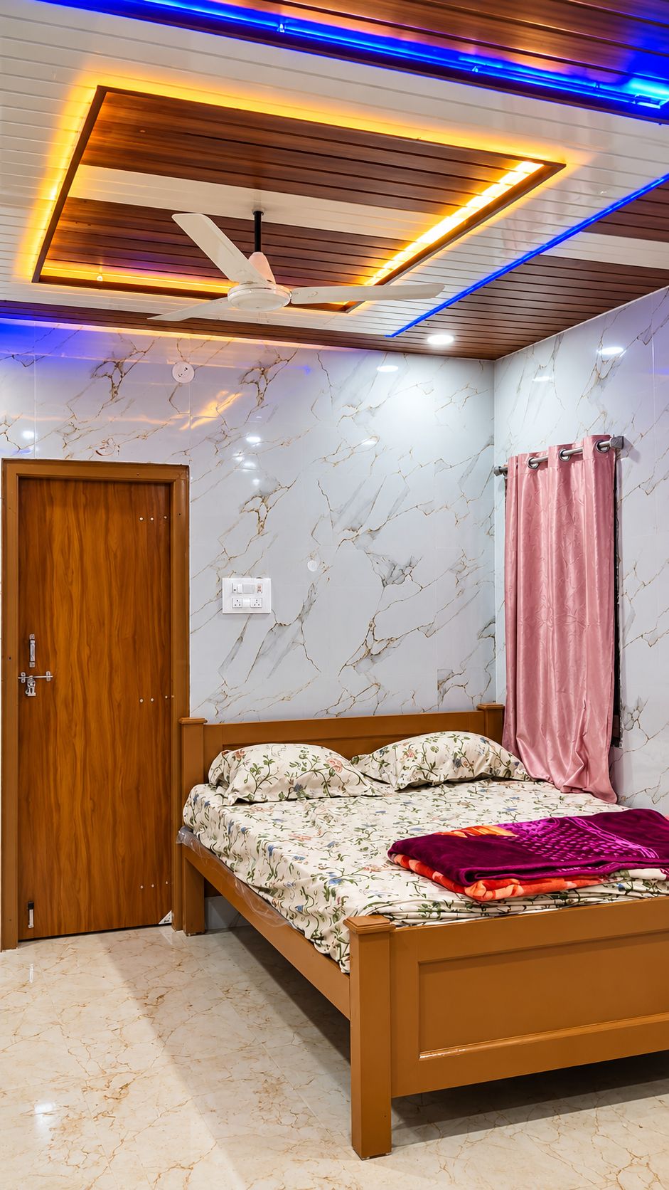Quarto com cama, porta de madeira, paredes com padrão marmorizado e teto com iluminação embutida.