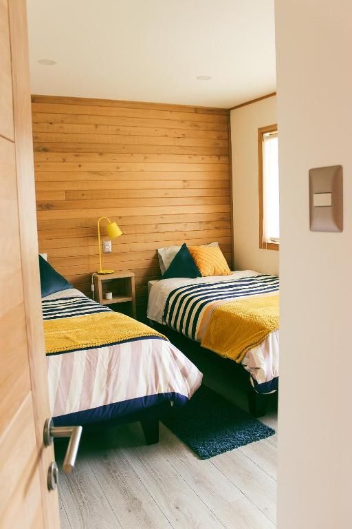 Quarto com duas camas, cabeceira de madeira, mesas de cabeceira e uma luminária.