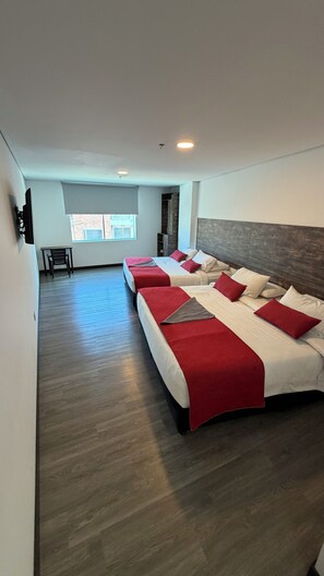 Quarto de hotel com uma cama grande, televisão e janela com vista para edifícios.