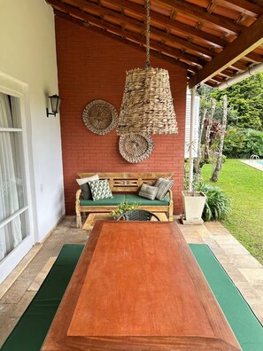 Um banco de madeira com almofadas, um candeeiro tecido pendente e um vaso com planta.