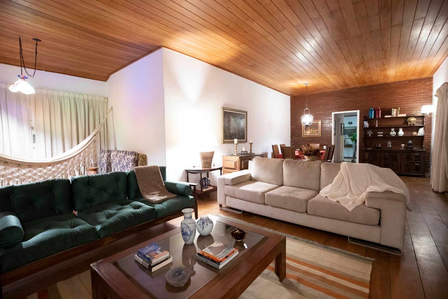 Uma sala de estar com um sofá verde, um sofá bege, teto de madeira e um espaço de jantar com mesa e cadeiras.