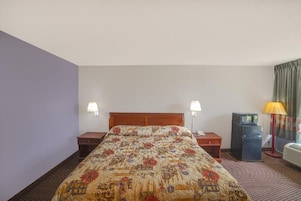 Quarto de hotel com cama, duas mesas de cabeceira, um frigorífico e uma lâmpada.
