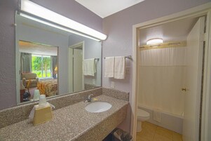 Casa de banho com bancada de granito, lavatório branco, espelho e zona de duche.