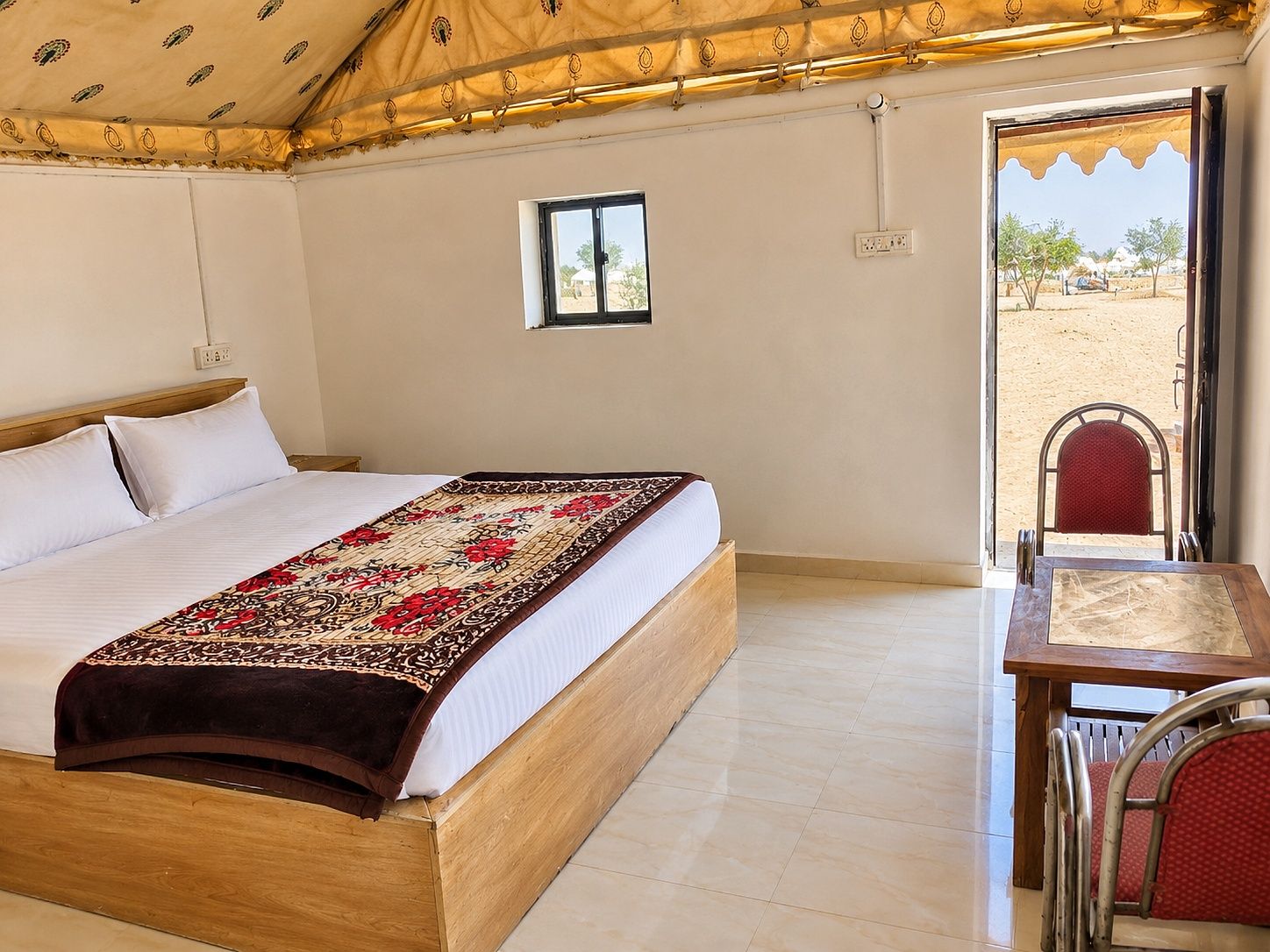 Quarto com cama, uma pequena mesa e uma cadeira. Há uma janela com vista para o exterior.