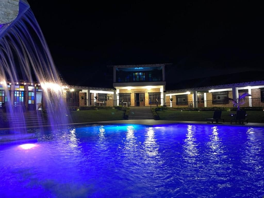 Vista noturna de um hotel com piscina e fonte.
