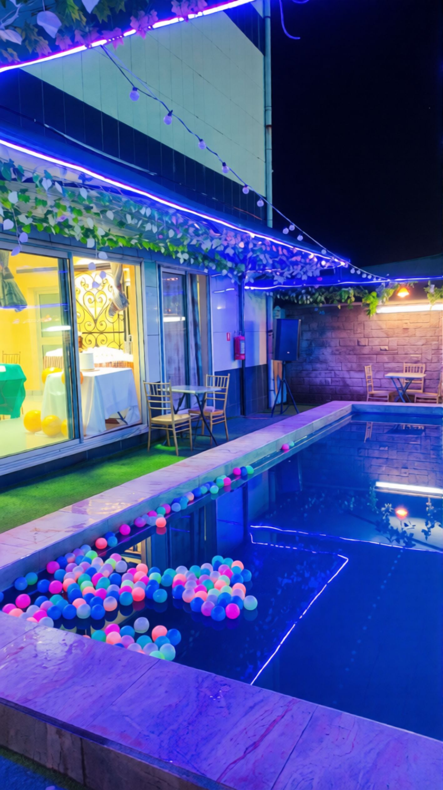 Área de piscina com fonte, espaço de estar com cadeiras e um edifício com porta de vidro.