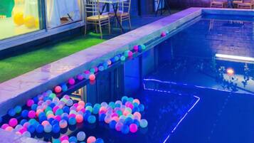 Área de piscina com fonte, espaço de estar com cadeiras e um edifício com porta de vidro.
