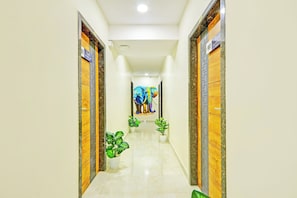 Corredor de hotel com portas de madeira, piso de mármore e um mural de elefante colorido na parede.
