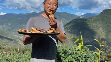 Uma pessoa segura um prato com comida, em um ambiente natural com montanhas ao fundo.