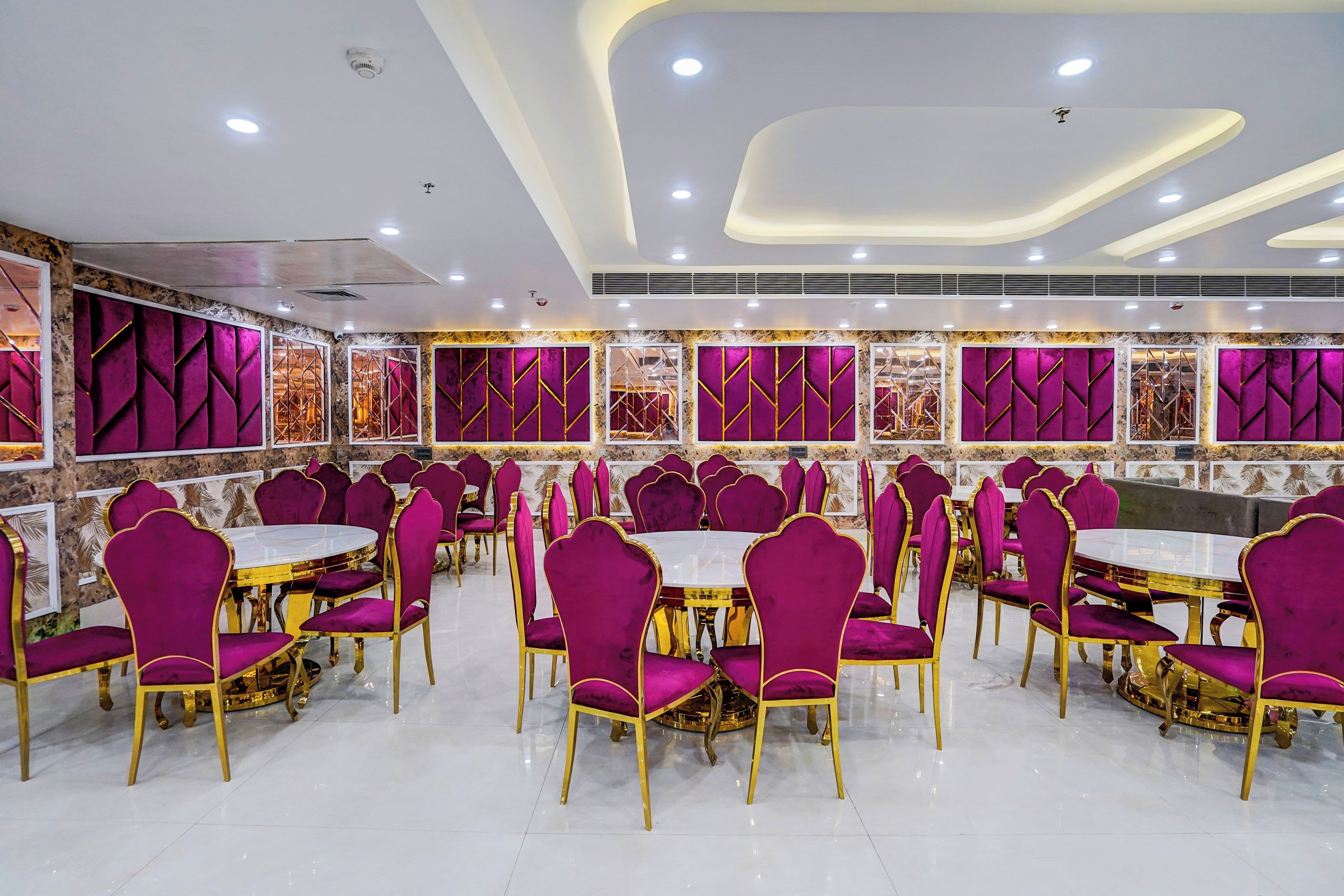 Interior de restaurante com paredes de mármore, cadeiras estofadas em roxo e mesas com detalhes dourados.