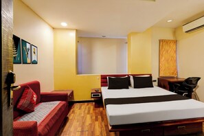 Quarto de hotel com cama, escrivaninha, cadeira, sofá vermelho e obras de arte na parede.