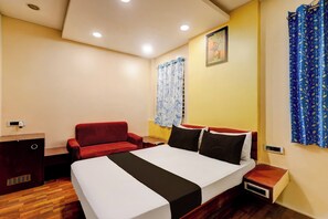 Quarto de hotel com cama, sofá vermelho, mesa pequena e aquecedor fixado na parede.