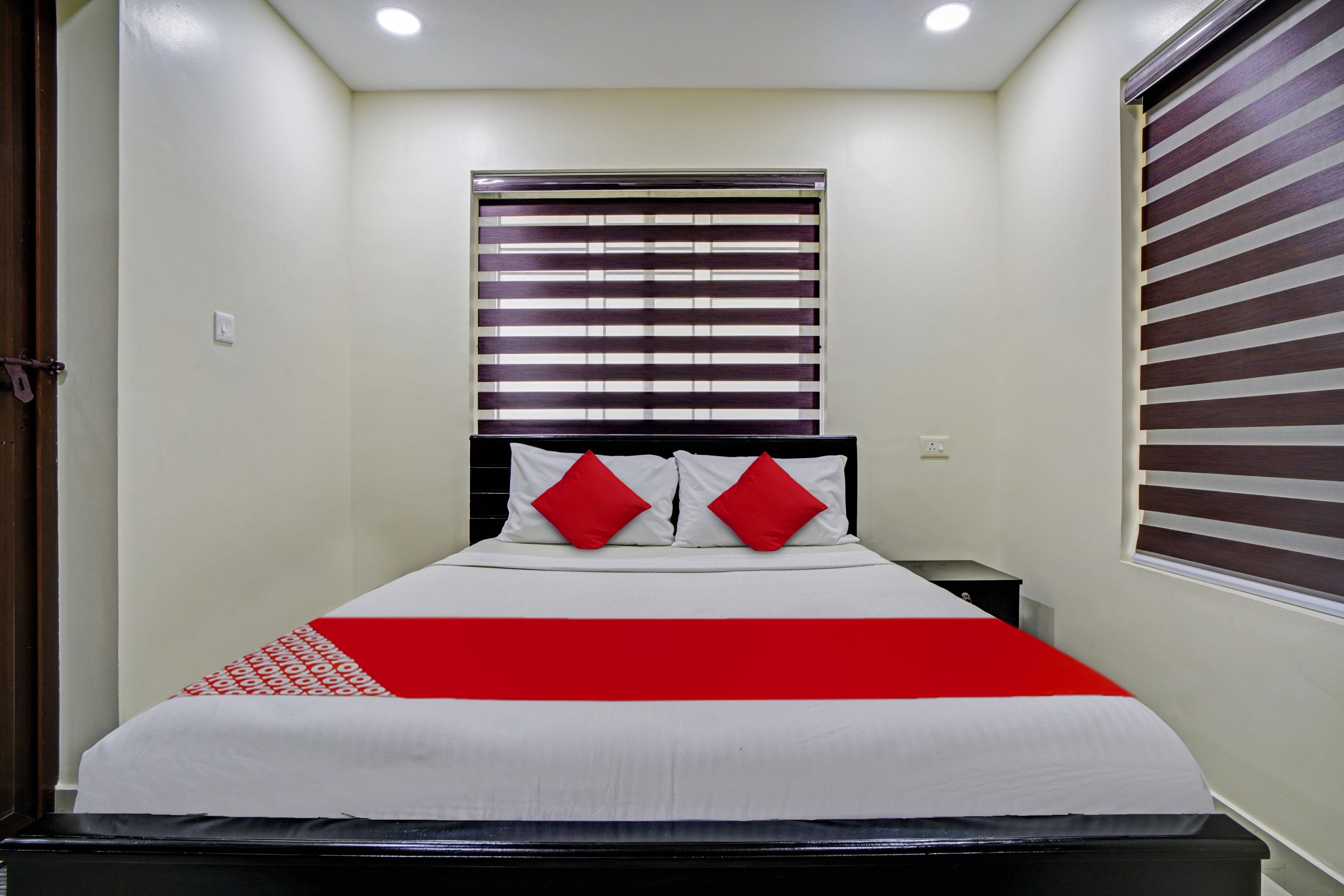 Um quarto com cama, duas mesas de cabeceira, uma janela com persianas e uma porta.