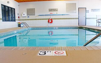 Piscina interna com cadeira de salva-vidas, aviso de proibição de mergulho e indicação de limite máximo de pessoas.