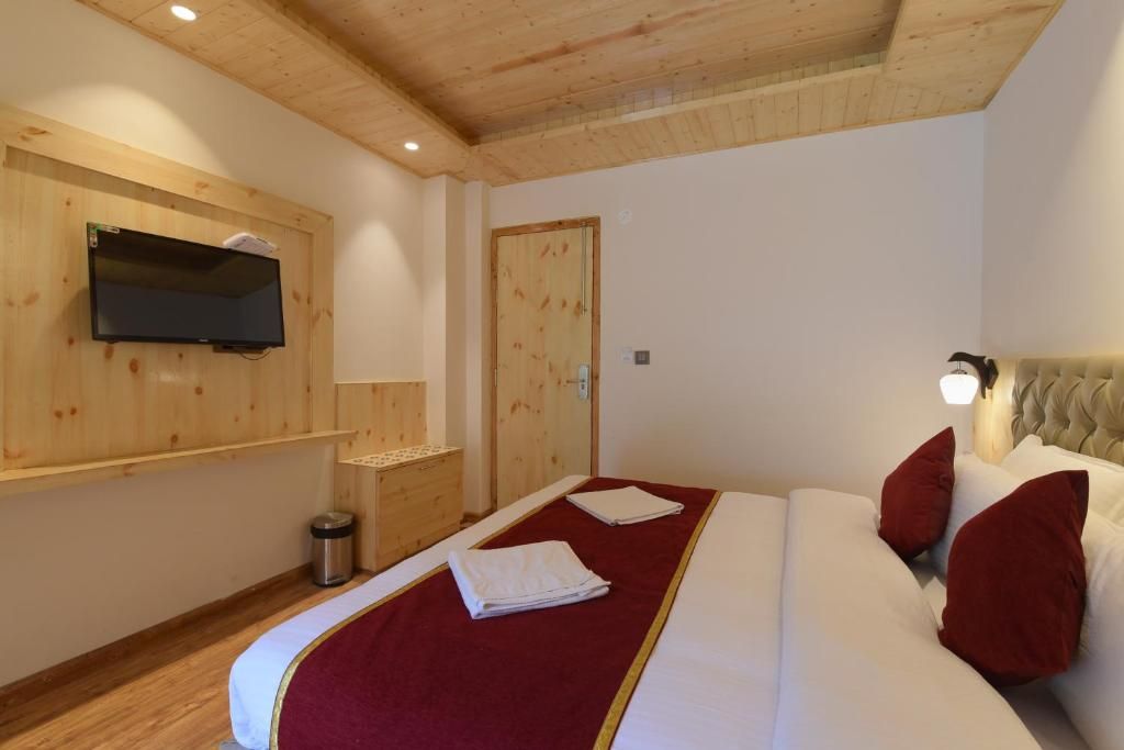 Quarto com cama, televisão na parede, porta de madeira e lixeira.