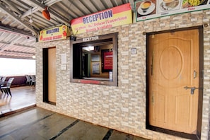 Uma área de recepção com placa indicando quartos disponíveis, um balcão de atendimento e uma porta de madeira.