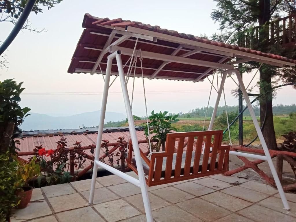 Um baloiço de madeira com estrutura de metal, um banco e um terraço com tijoleira e plantas em vasos.