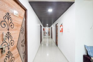 Corredor com porta de madeira à esquerda, extintor de incêndio à direita e chão em azulejo.