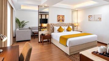 Quarto de hotel com cama, escrivaninha, cadeira, sofá, televisão e planta.