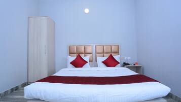 Quarto de hotel com uma cama, guarda-roupa, mesa de cabeceira com telefone e luminária no teto.