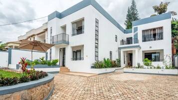 Uma casa moderna de dois andares com um pátio pavimentado, uma varanda e um jardim com diversas plantas.