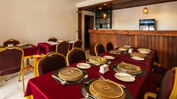 Uma área de refeições com mesas preparadas para o serviço, cadeiras e um bar com balcão.