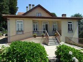 Uma casa de dois andares com varanda, escadaria e jardim.