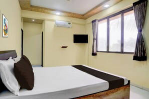 Quarto de hotel com cama, televisão, janela com cortinas e ar condicionado.