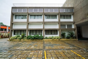 Edifício de vários andares com telhado plano, grandes janelas e um pátio pavimentado com plantas.