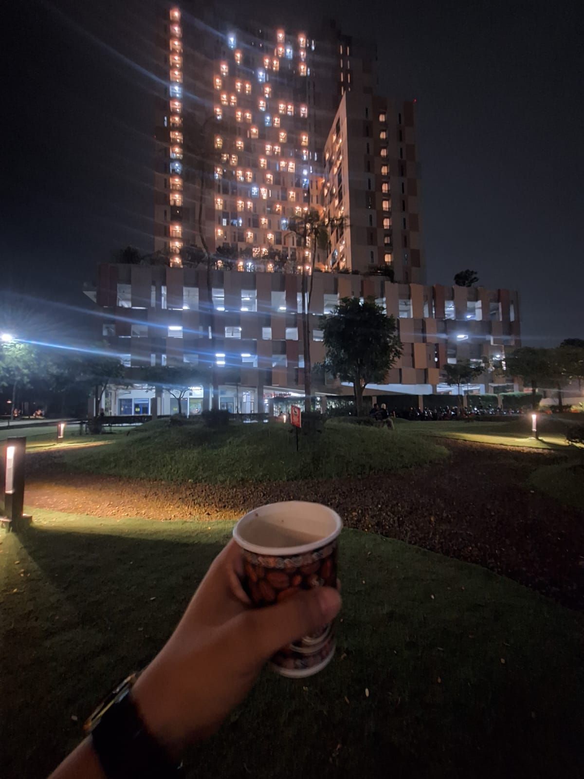 Uma pessoa segurando uma xícara, com um edifício moderno ao fundo.
