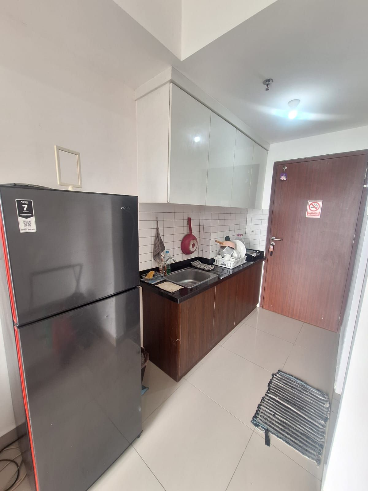 Cozinha compacta com geladeira preta, armários brancos e bancada de madeira.