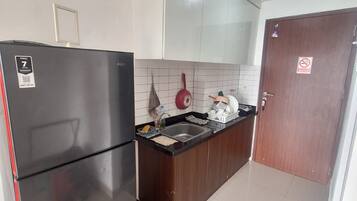 Cozinha compacta com geladeira preta, armários brancos e bancada de madeira.