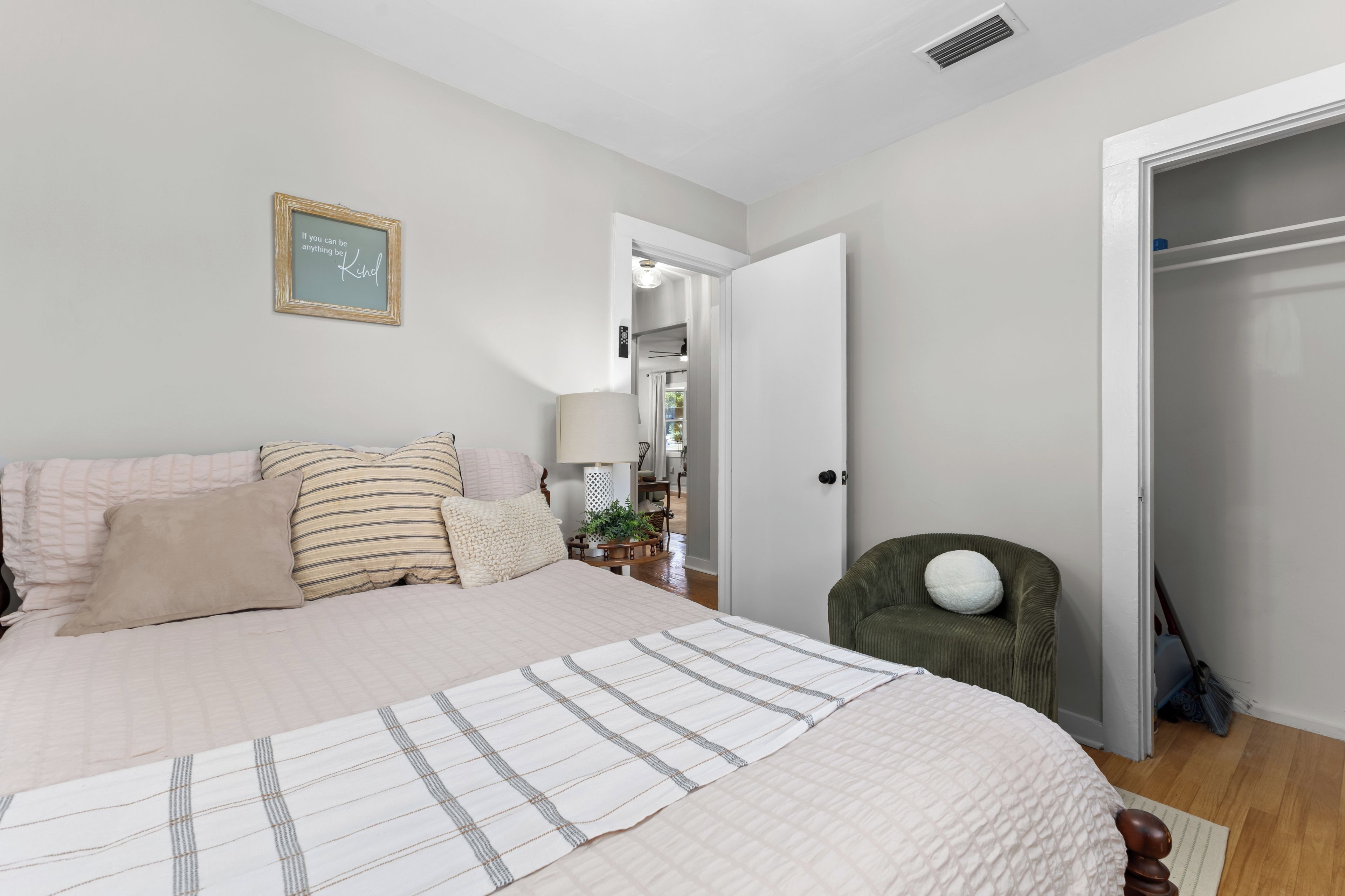 Quarto com cama, uma cadeira, porta e parede com uma moldura de frase.