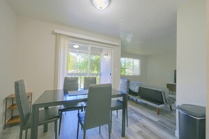 Uma área de refeições com mesa de vidro e cadeiras, um sofá e uma lixeira.