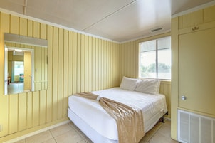 Quarto com uma cama de solteiro, janela com cortinas, porta e um espelho na parede.
