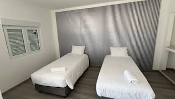 Quarto de hotel com duas camas de solteiro, uma janela com persianas e parede listrada.